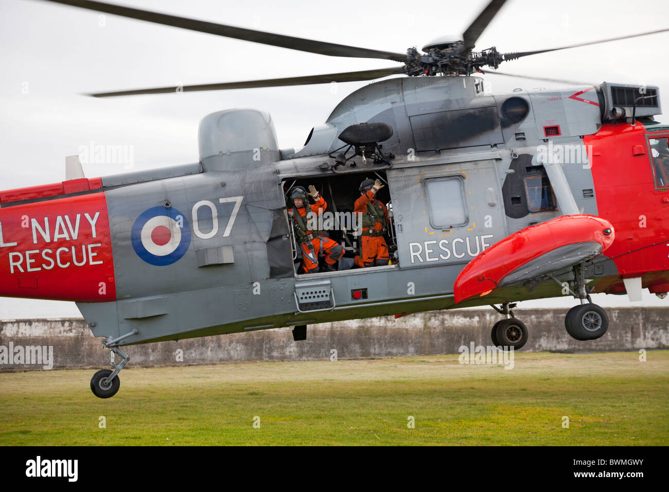Royal Navy rescue helicopter taking off from grass on the shorefront of ...