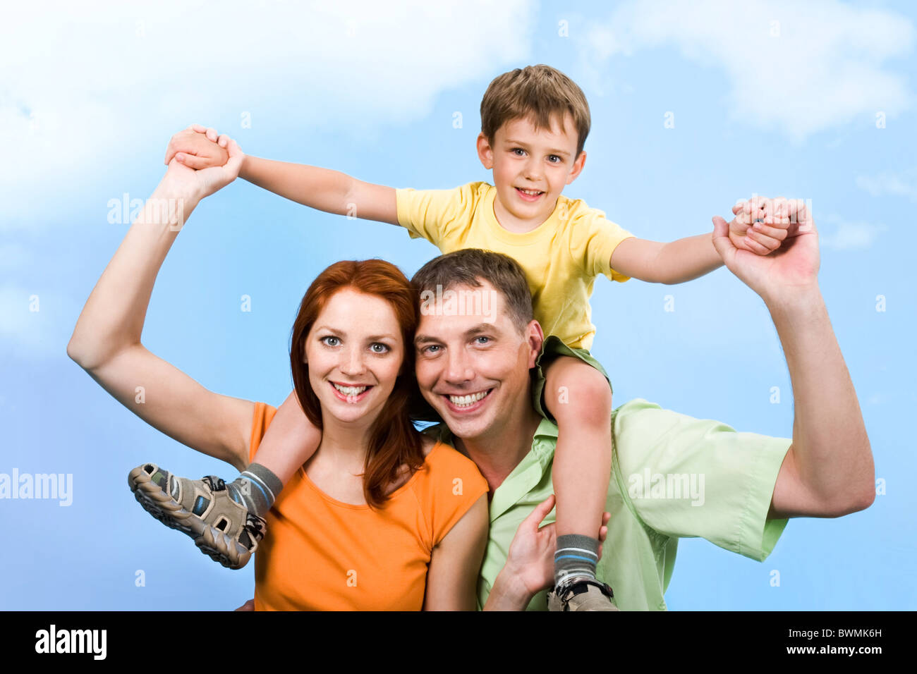 Photo of little boy sitting on parents’ shoulders on a blue background ...