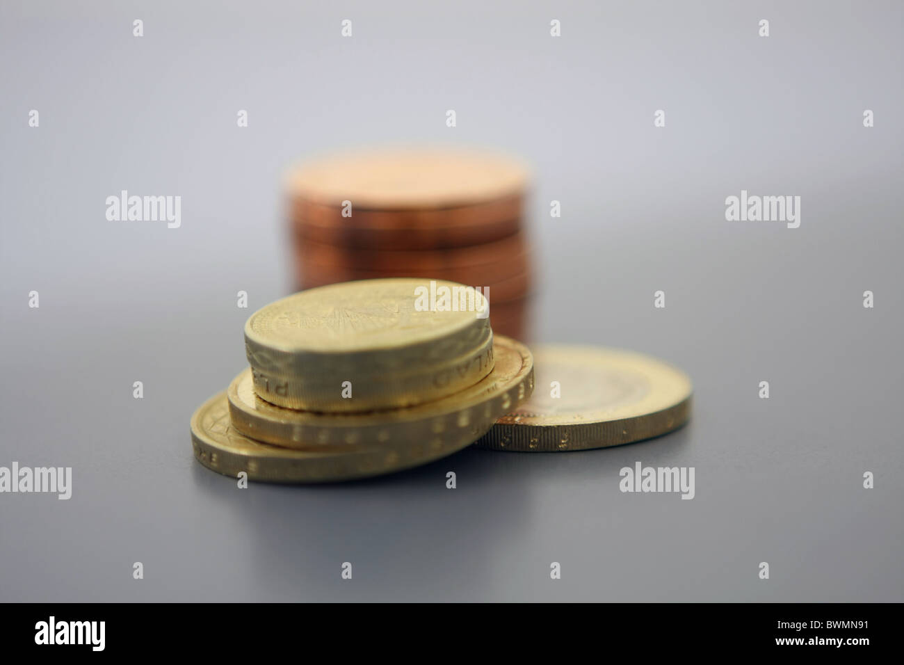 two Sterling £1 coins on £2 coins in front of a stack of out of focus ...