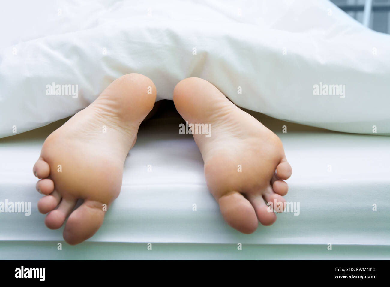 Image of bare feet pointing out of white linen blanket Stock Photo - Alamy