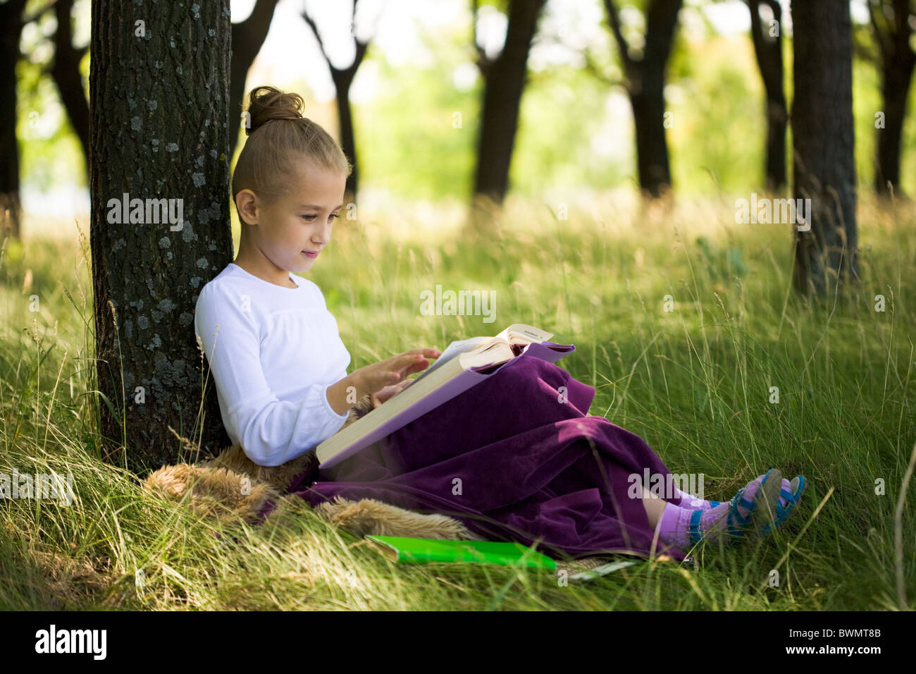Pretty girl sitting under tree and reading at summer in a park Stock ...