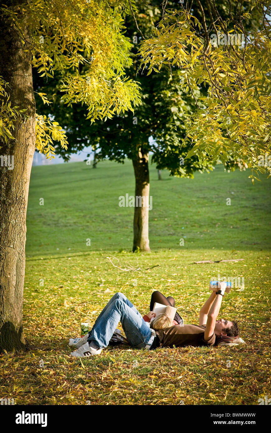 Couple reading under tree in park Stock Photo - Alamy