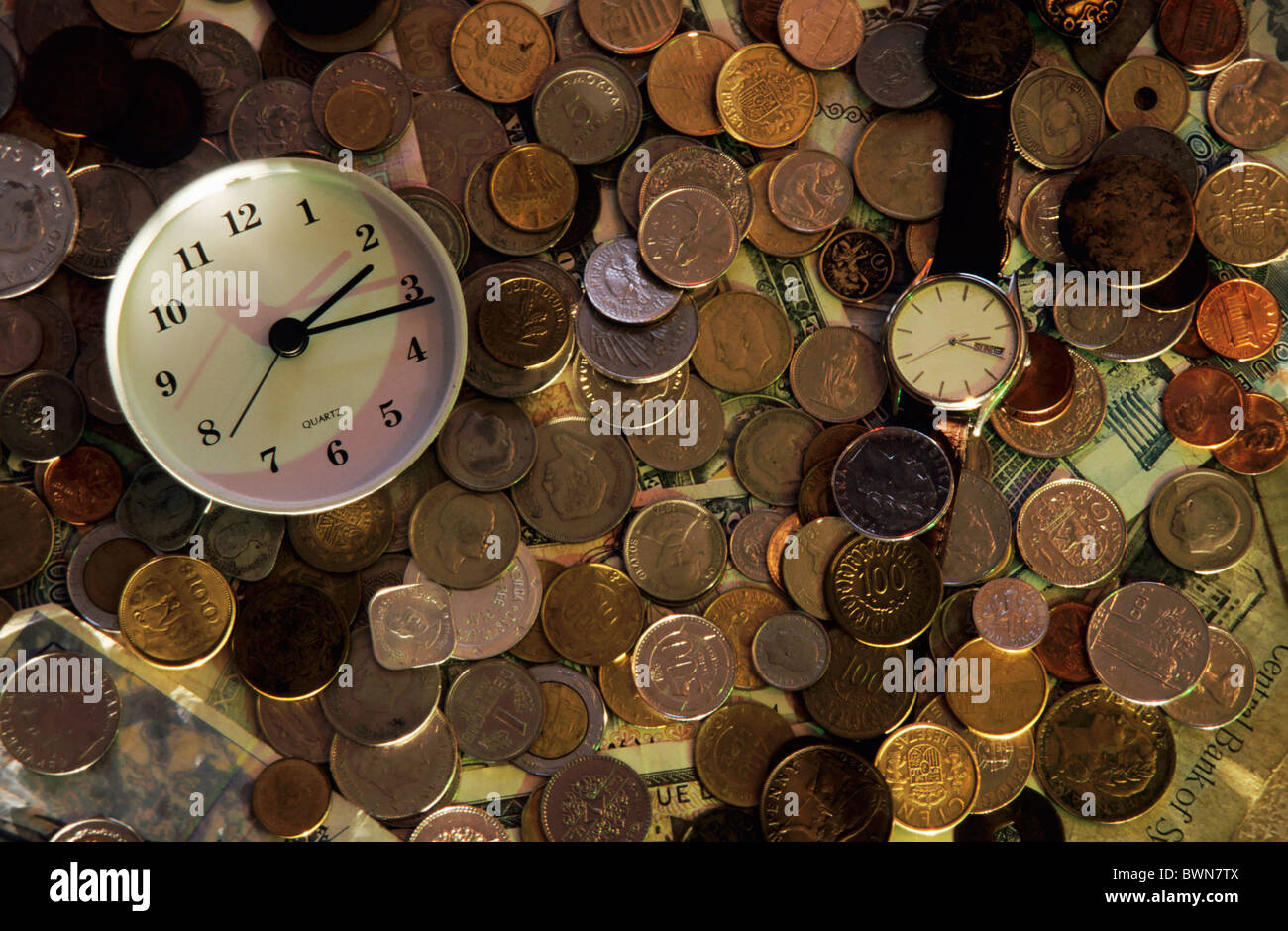 Clock and a wristwatch on a bed of international coins Stock Photo - Alamy