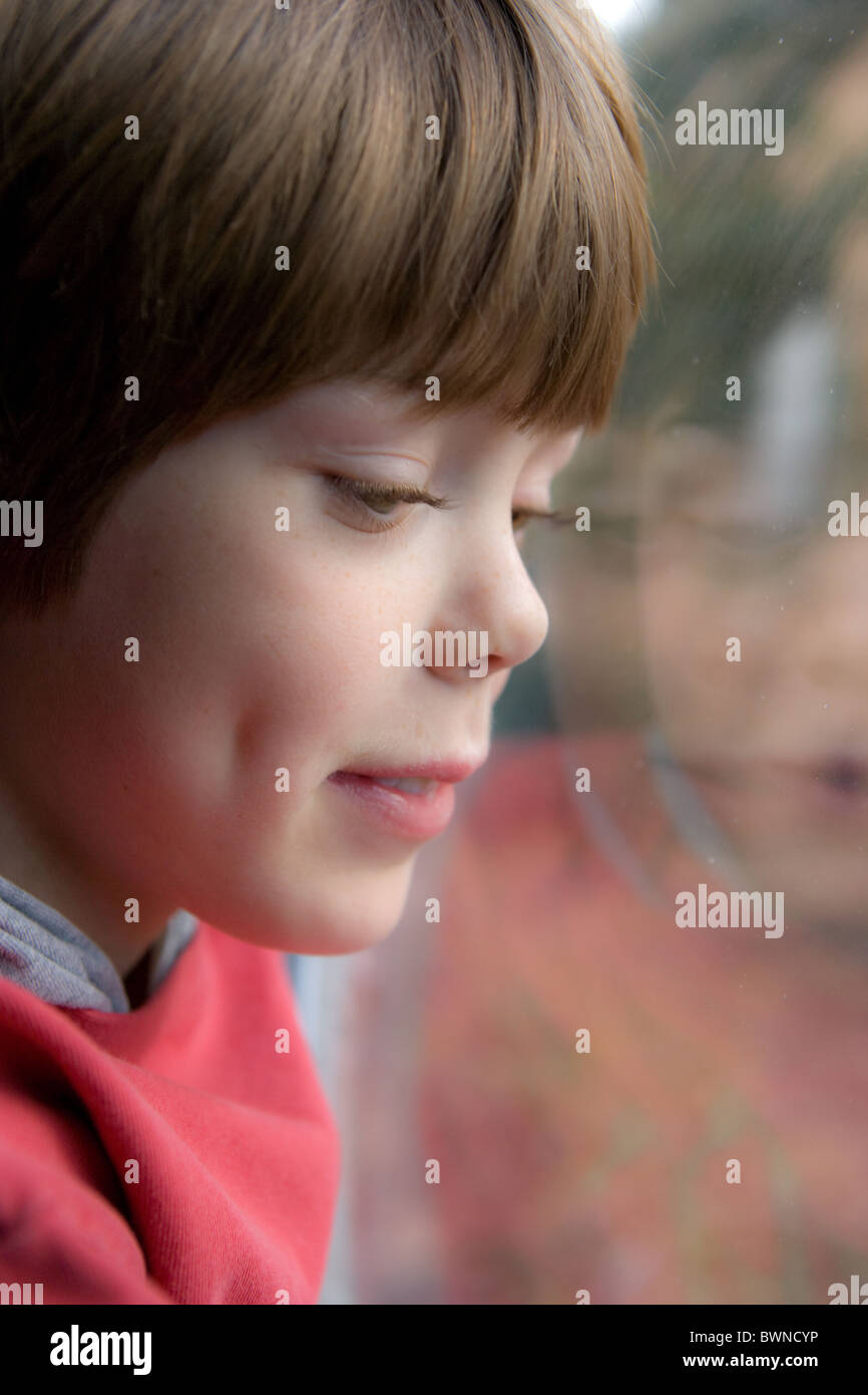 Young boy looking down next to a window Stock Photo - Alamy