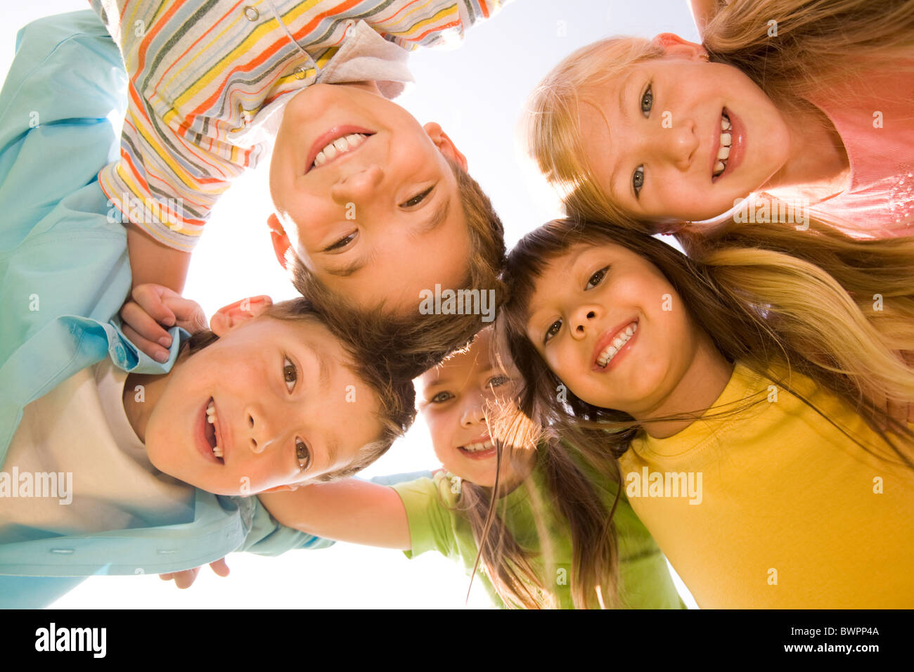 Below view of happy children embracing each other and smiling at camera ...
