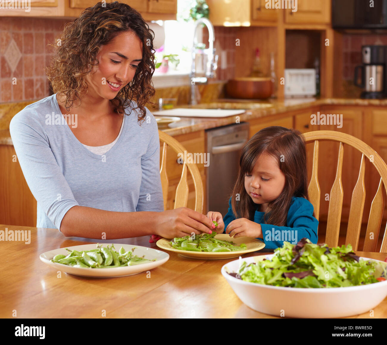 Mother and daughter shelling peas at dining table Stock Photo - Alamy