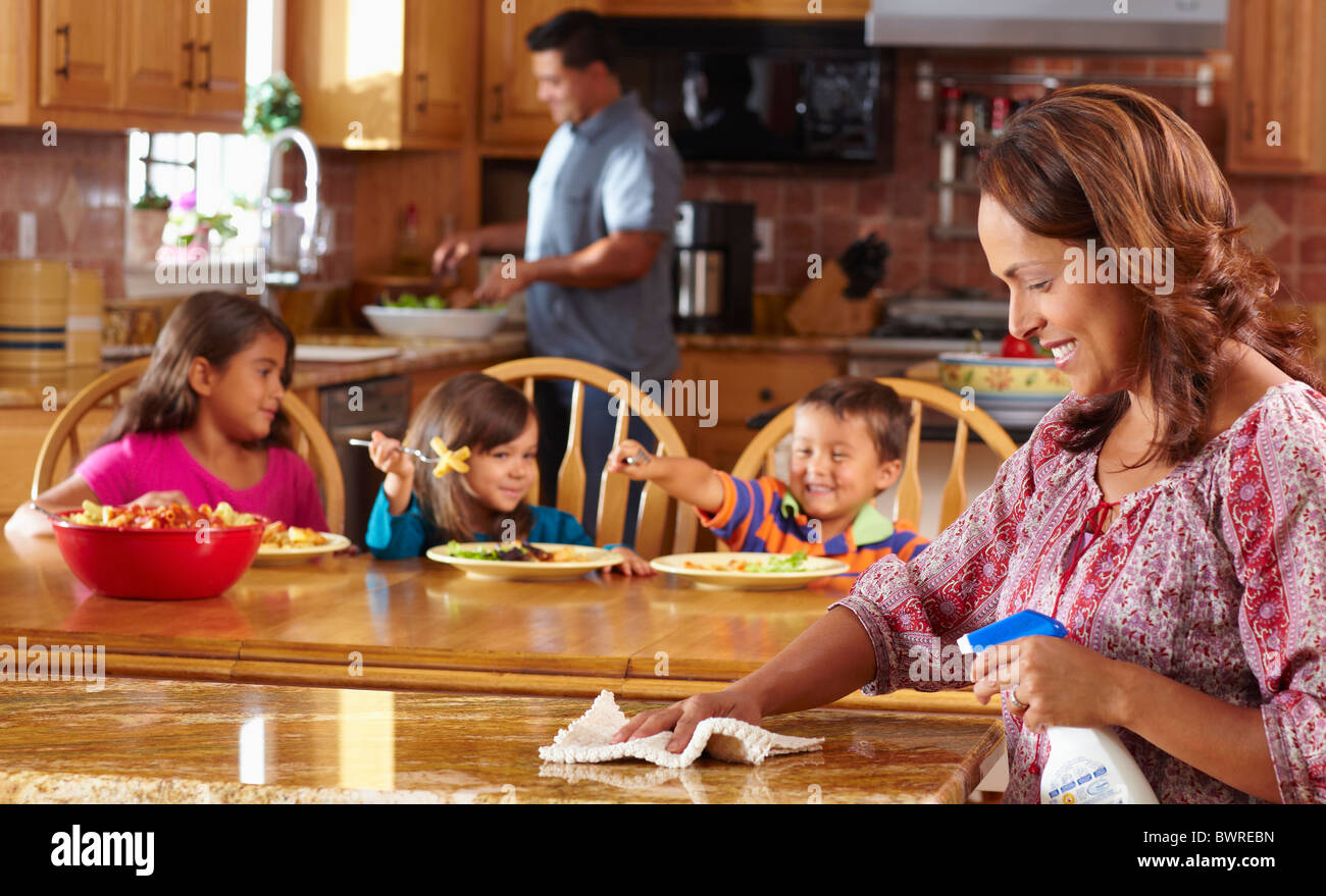 Mother cleaning while children eat in background Stock Photo - Alamy