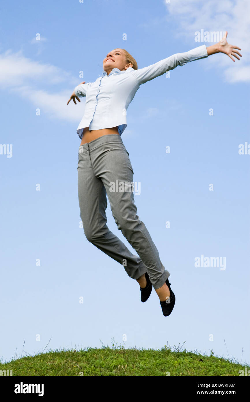 Portrait of happy female jumping over green grass against blue sky ...
