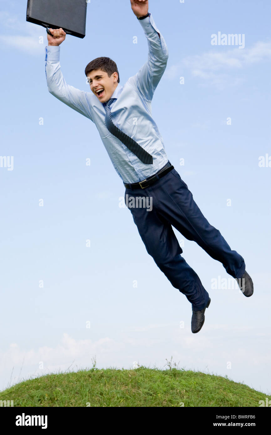 Handsome businessman leaping over green grass with blue sky at ...