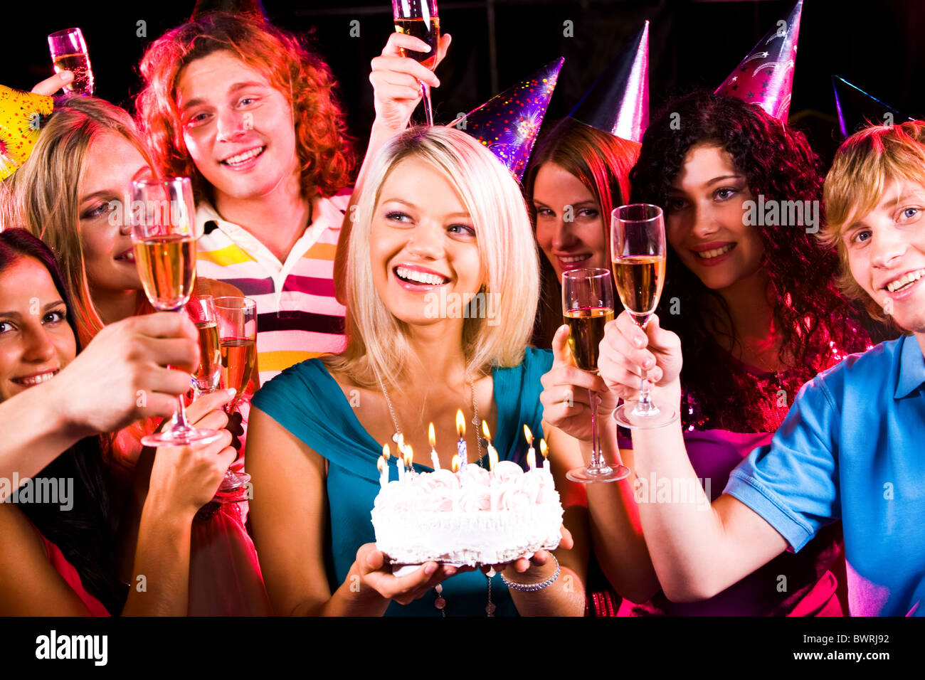 Portrait of joyful girl holding birthday cake surrounded by friends ...