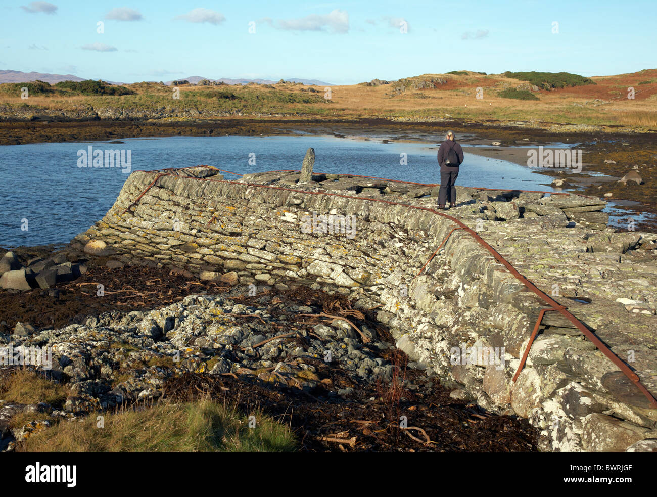 Damaged and disused Keills Jetty with female walker. Looking towards ...