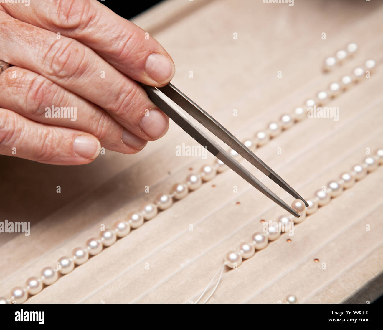 Close hand jeweler stringing pearls on a necklace Stock Photo - Alamy