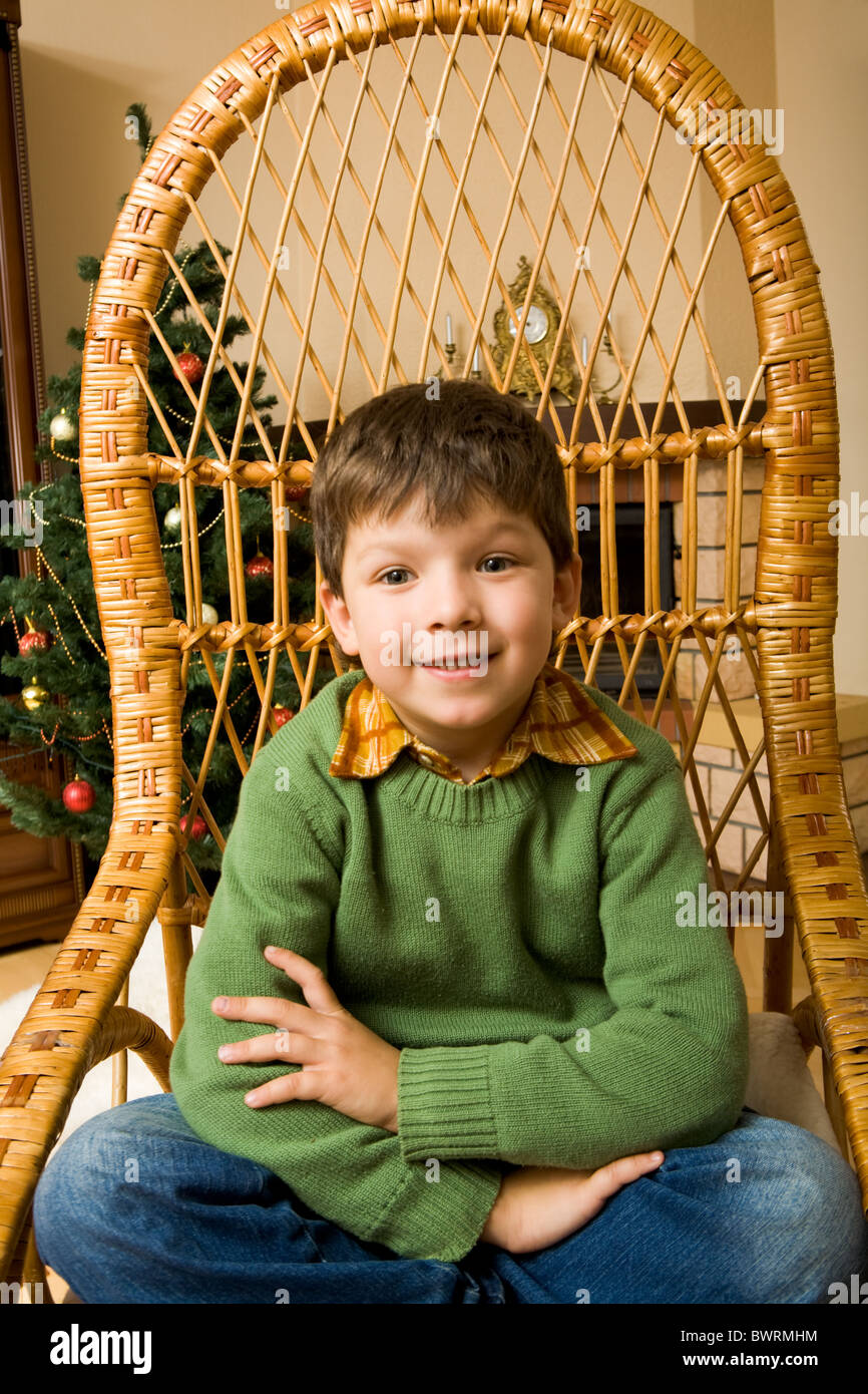 Portrait of boy sitting in wicker chair and looking at camera with ...