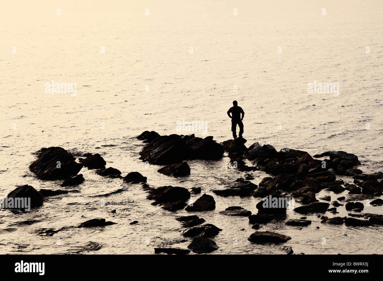 Lone figure standing on rocks looking at sea Stock Photo - Alamy