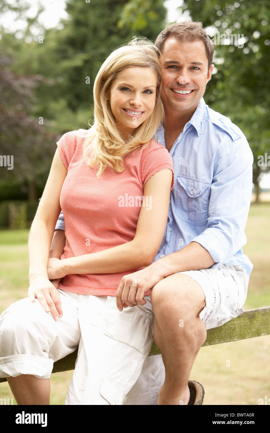 Couple Relaxing In Countryside Sitting On Fence Stock Photo - Alamy