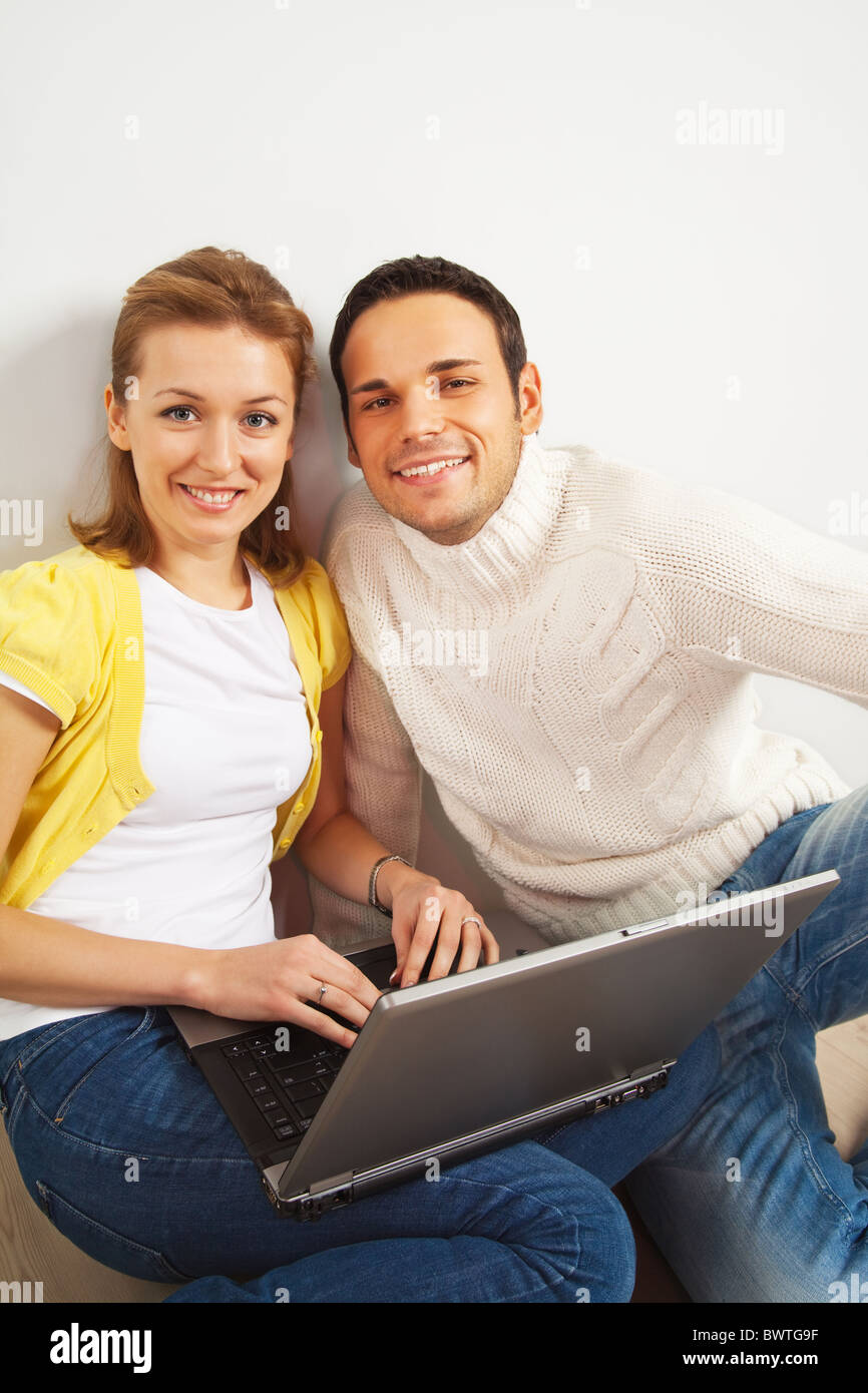 Happy young couple sitting on the floor with a laptop computer on their ...