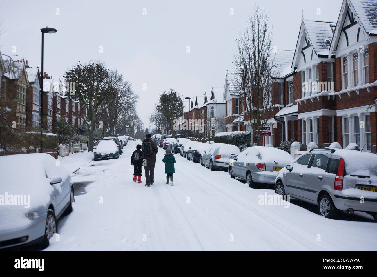 Family walk in centre of residential snowbound street in Dulwich, South ...