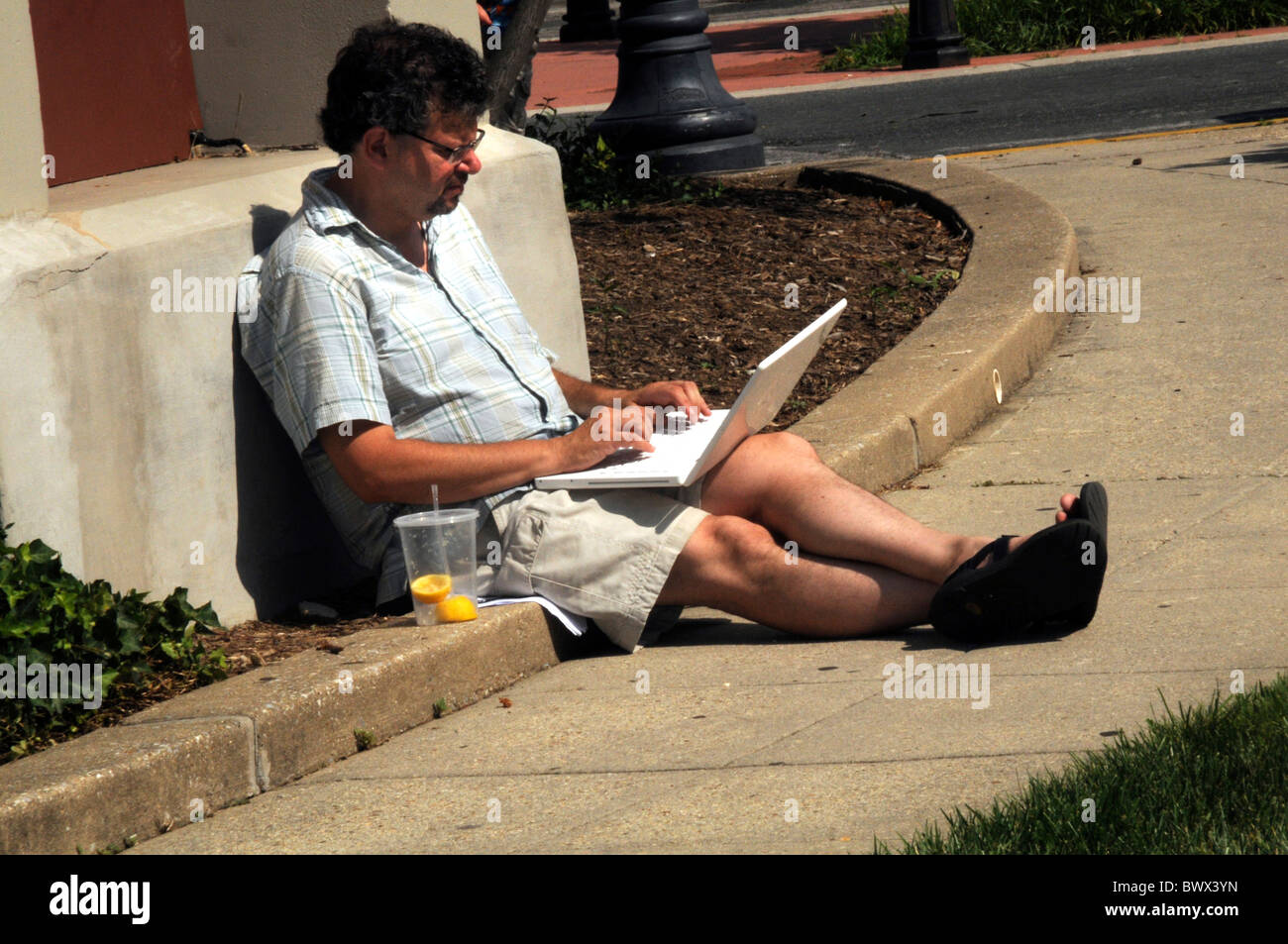 Young man sitting on the sidewalk working on his laptop computer in ...