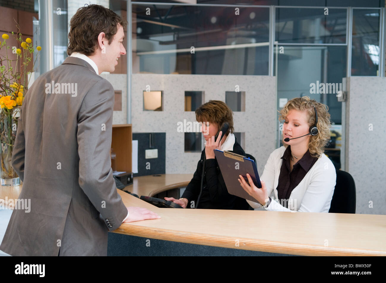 Client coming at the receptionist working at a helpdesk Stock Photo - Alamy