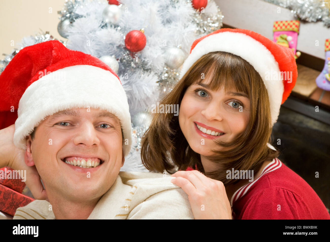 Portrait of happy husband and wife wearing Santa caps and looking at ...