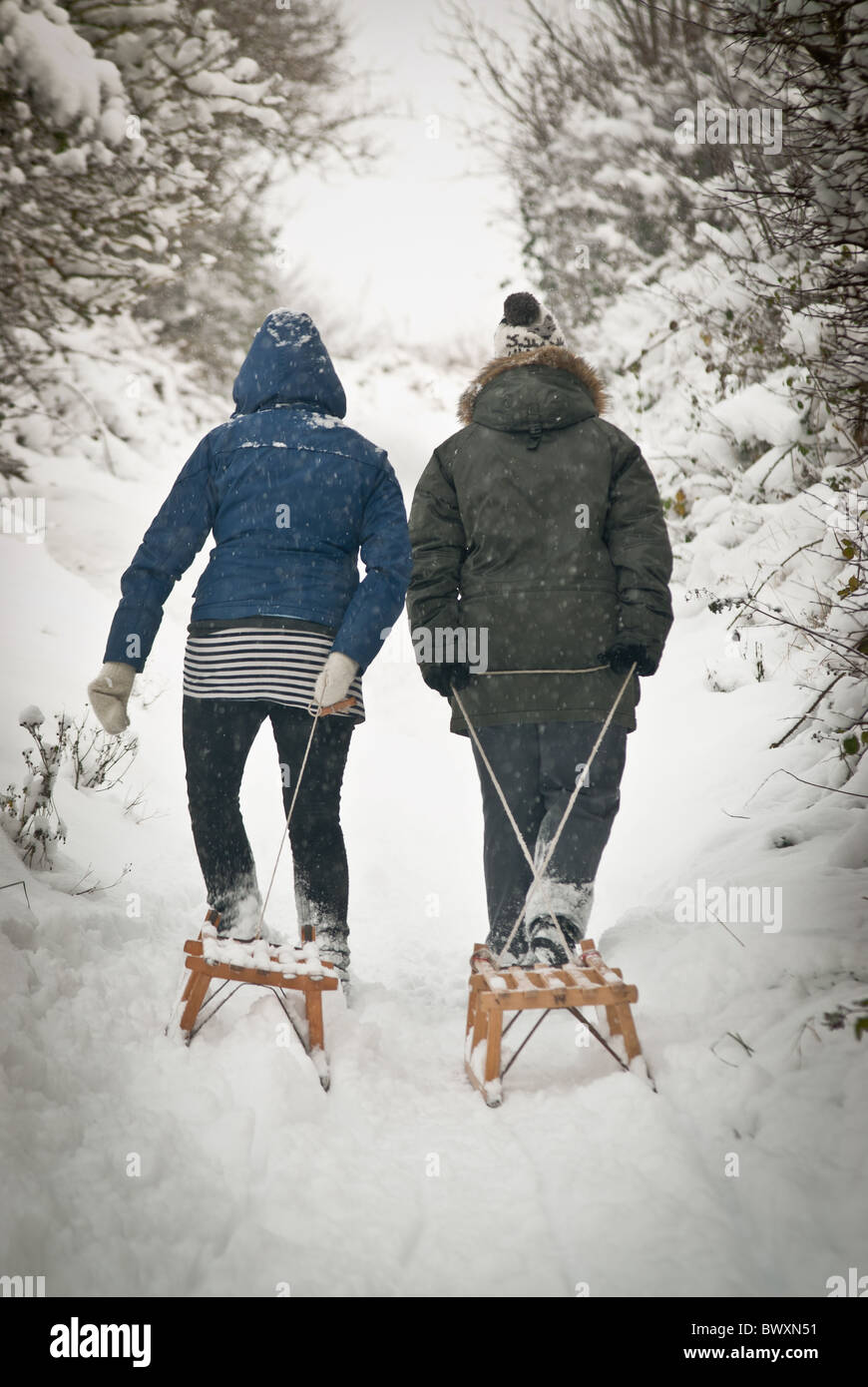 Two girls pulling toboggans up a country lane Stock Photo - Alamy