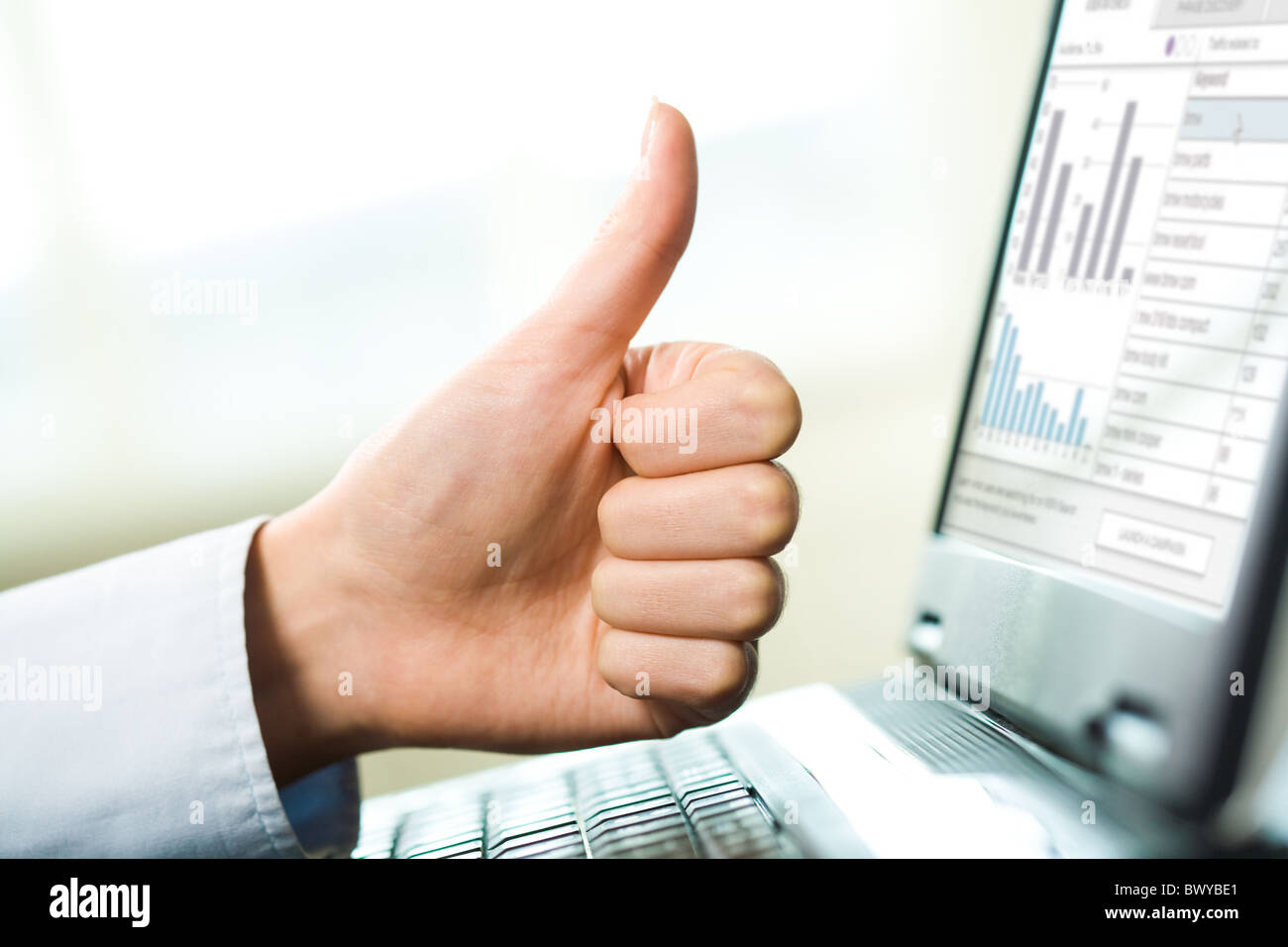 Close-up of female hand keeping thumb up over laptop screen on ...