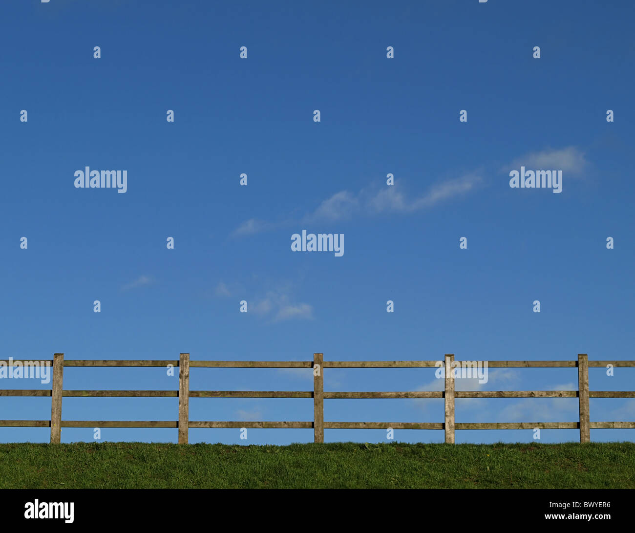 Rail fence on grass bank against blue sky with light clouds Stock Photo ...