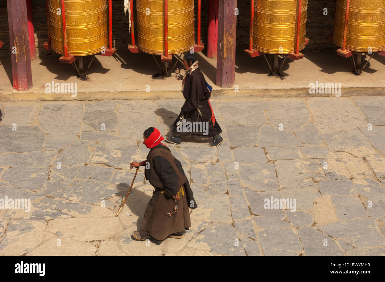 Pilgrims walking past gold gilded prayer wheels, Jokhang Monastery ...