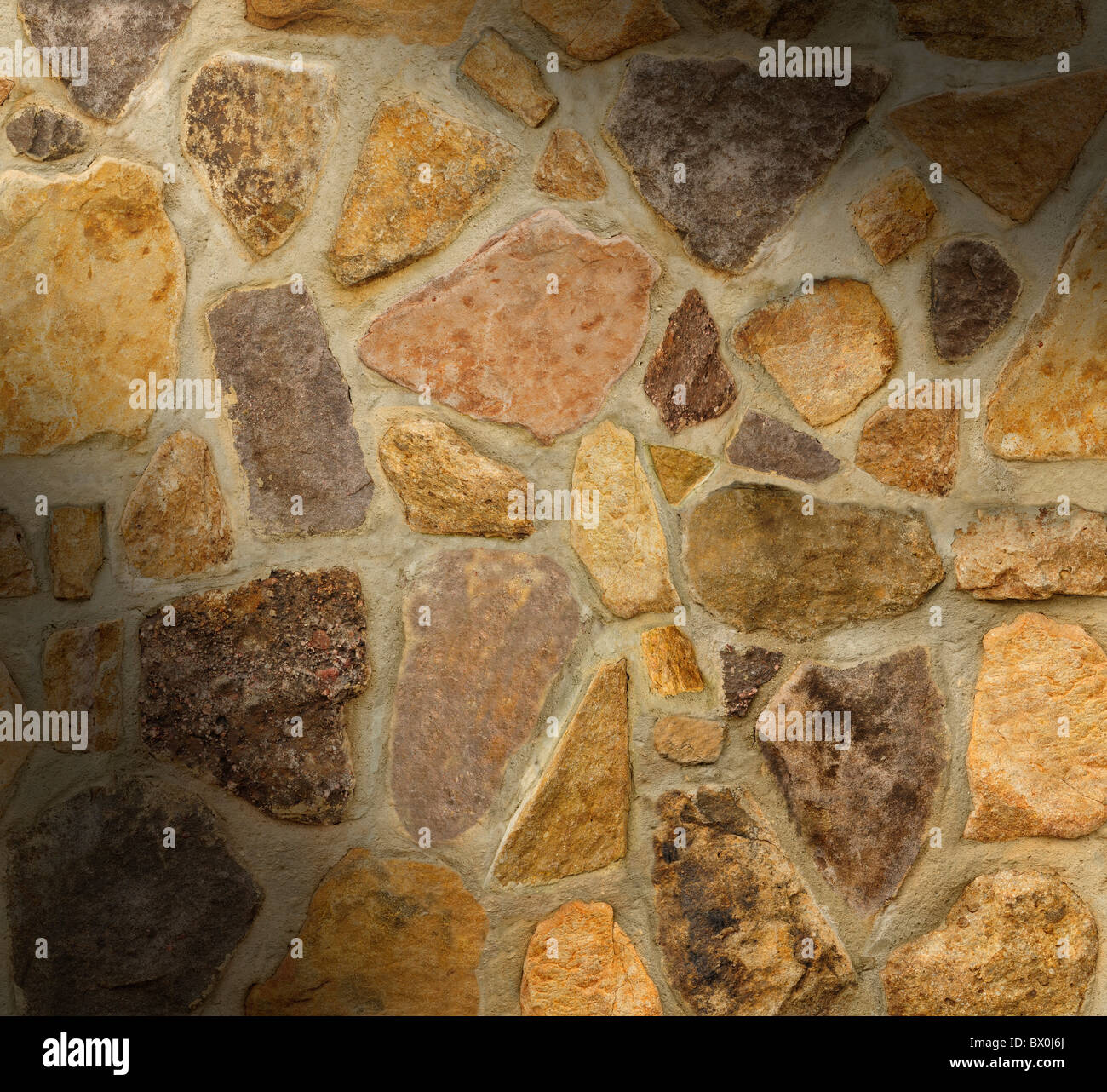 Masonry wall with irregular shaped stones dramatically lit diagonally ...