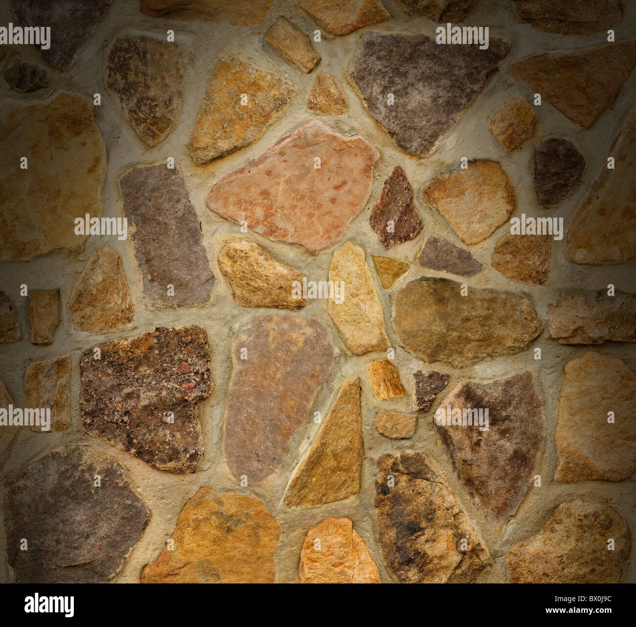 Masonry wall with irregular shaped stones dramatically lit from above ...