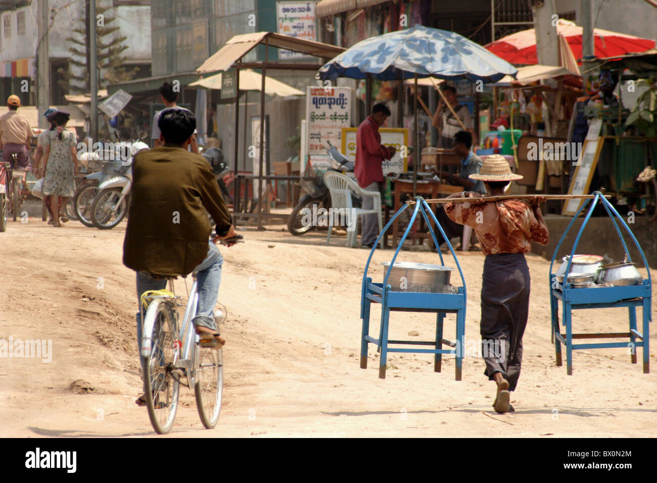A food seller who is walking and a man riding a bicycle share a dusty ...