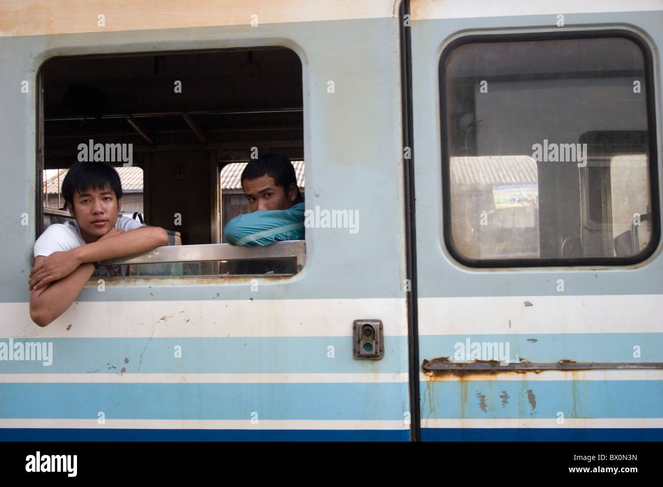 Two young Asian men are looking out of a railroad train passenger car ...