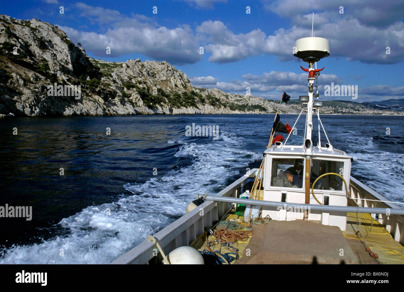 Fisherman steering a boat in the sea with coastline visible in the ...