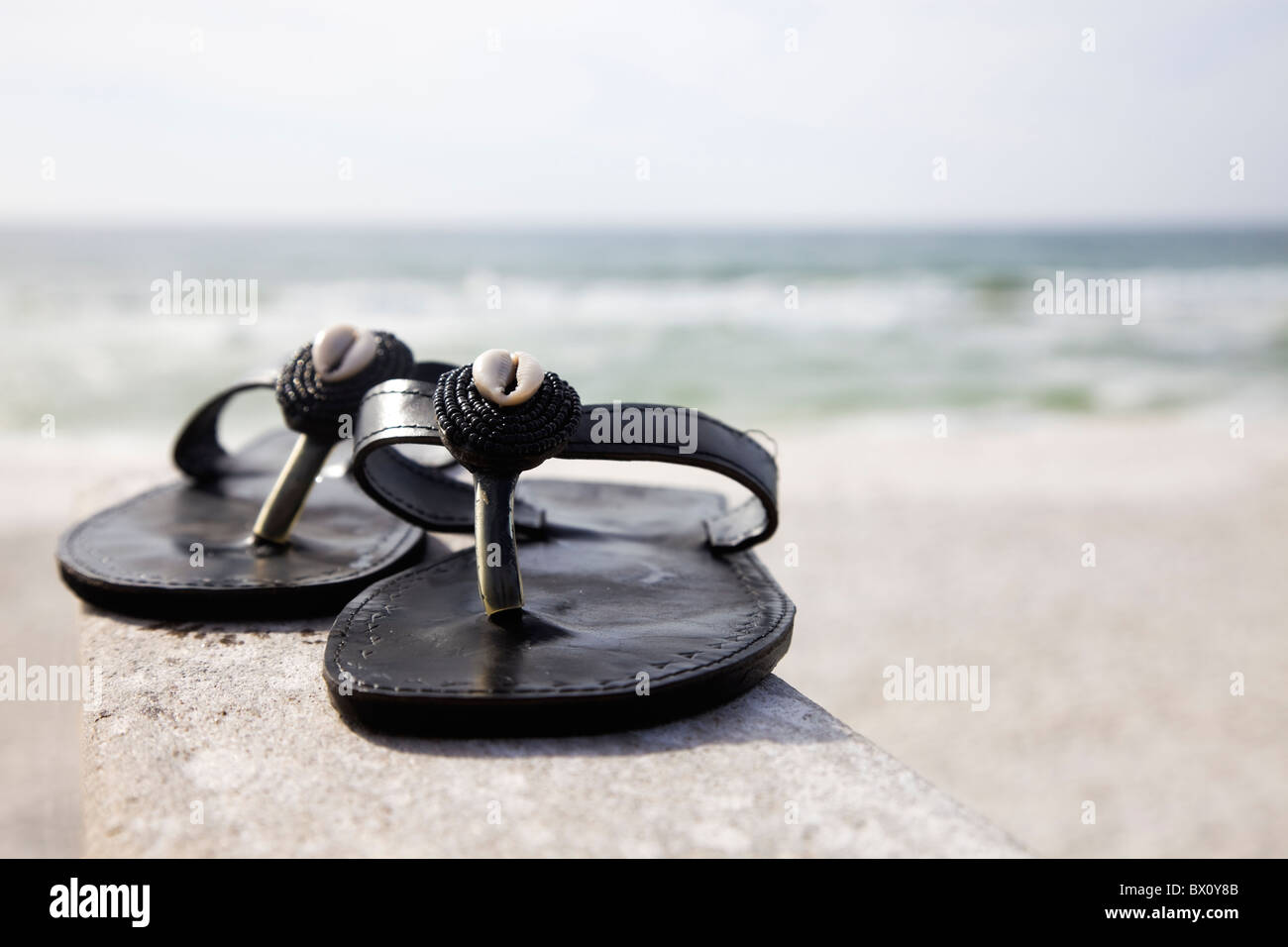 Black flip flops with shells on the beach Stock Photo - Alamy