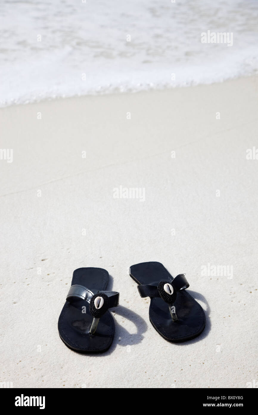Black flip flops with shells on the beach Stock Photo - Alamy