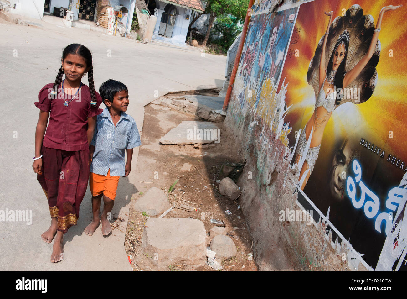 Indian children walking past a Telegu movie poster in an indian street ...