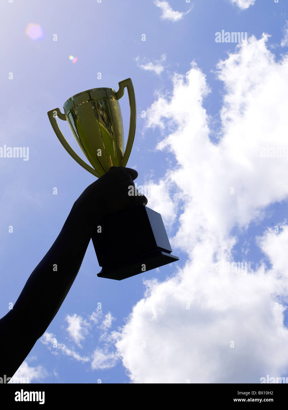 A victorious person holds up a large, gleaming trophy cup, silhouetted ...