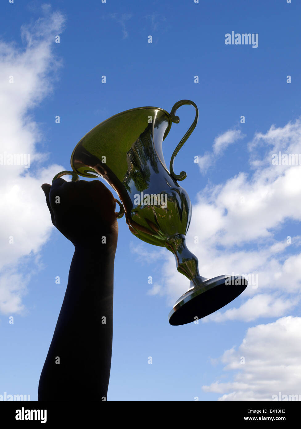 A victorious person holds up a large, gleaming trophy cup, silhouetted ...