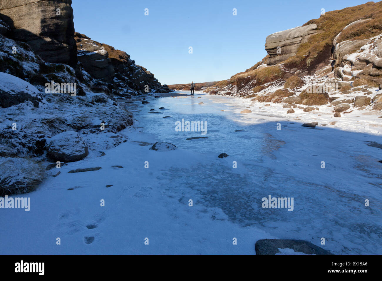A walker on the Kinder River in winter on Kinder Scout in the Dark Peak ...