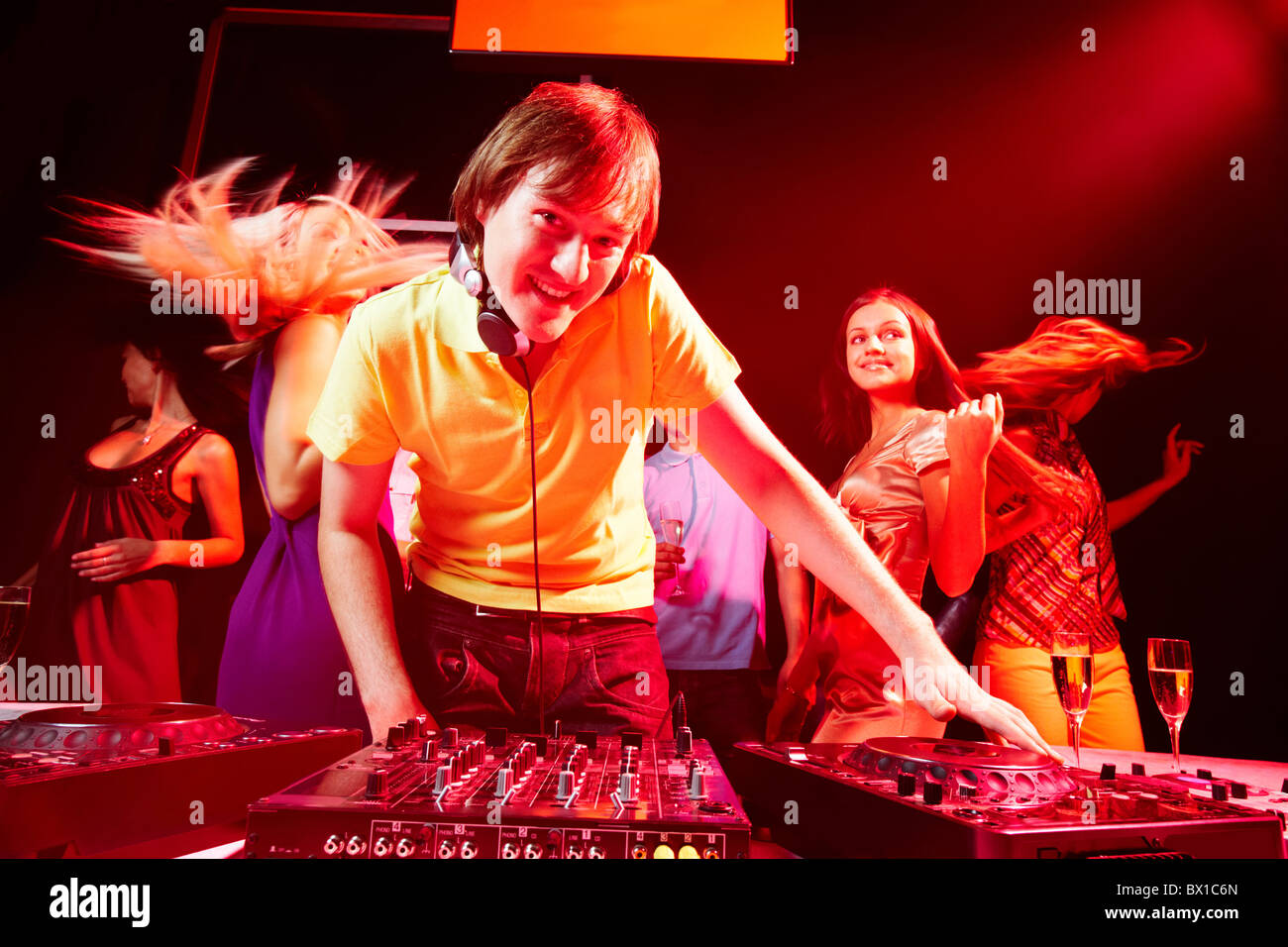 Portrait of handsome deejay looking at camera with dancing teens on ...