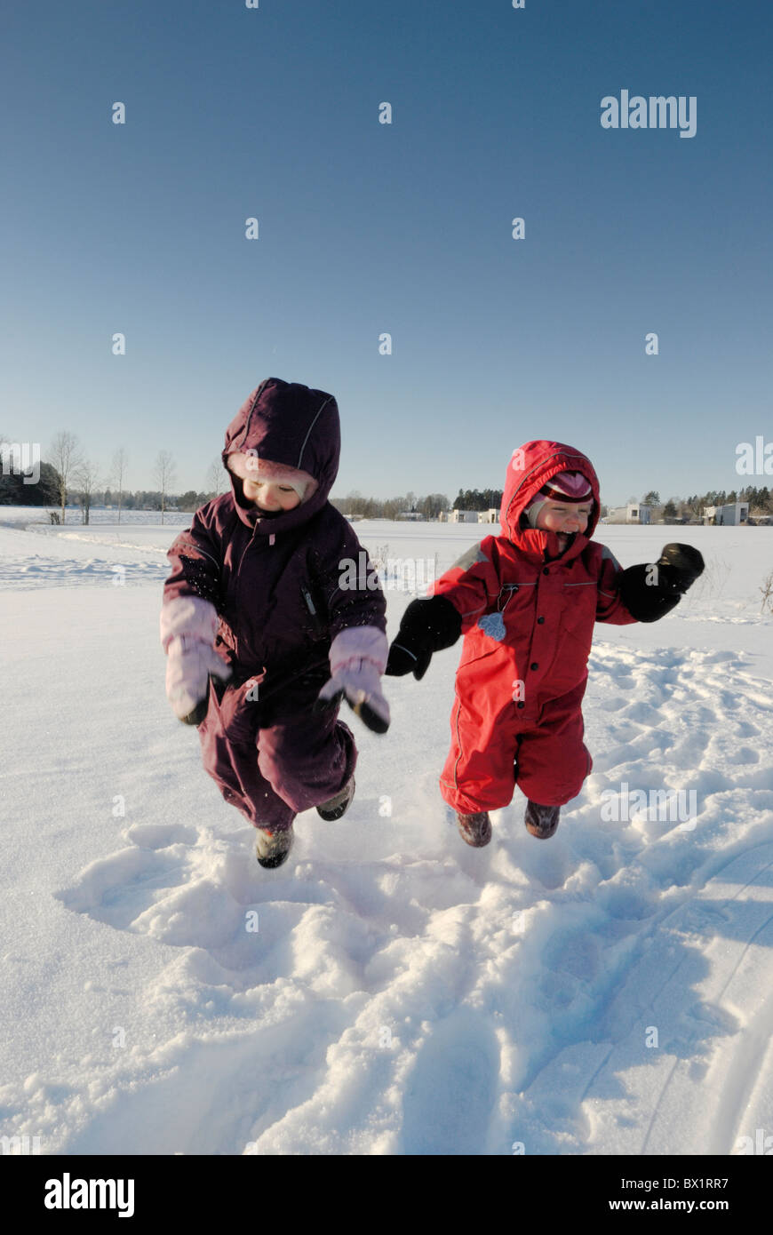 Two kids jumping in snow Stock Photo - Alamy