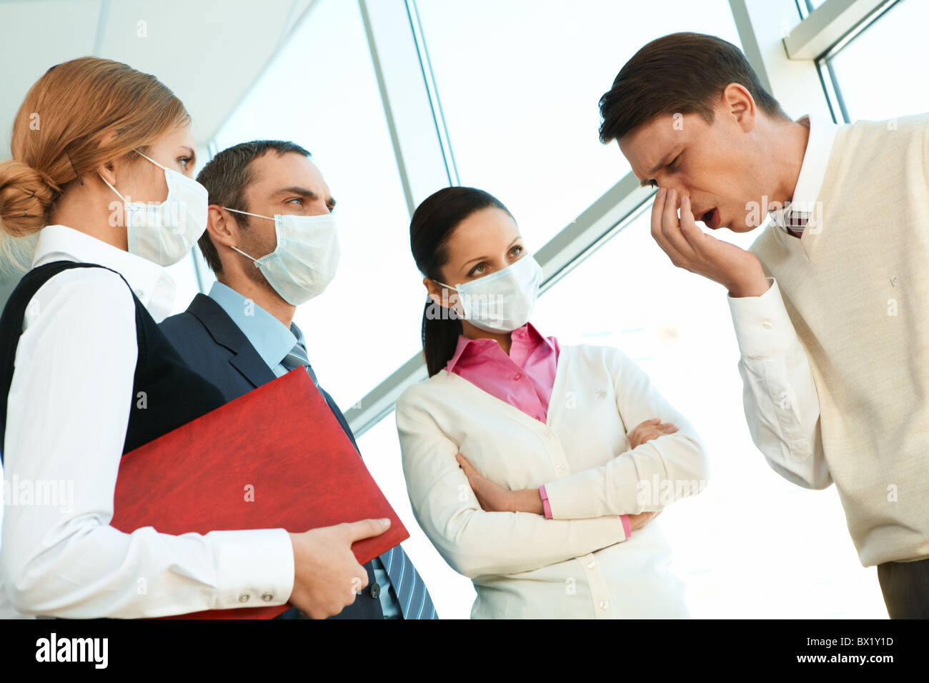 Group of co-workers in protective masks looking strictly at sneezing ...