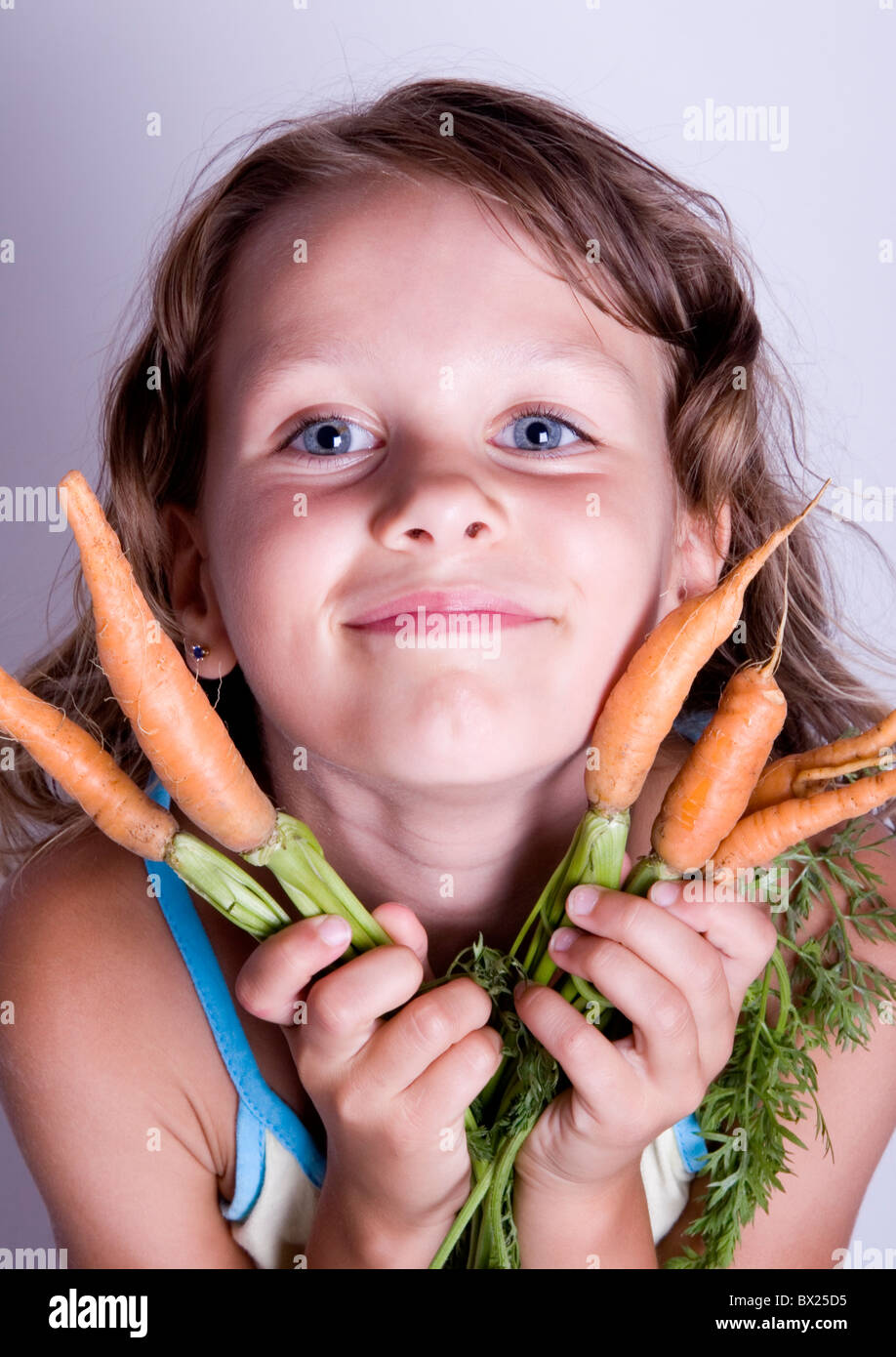A sweet young girl eating fresh carrots. The child is on a white ...