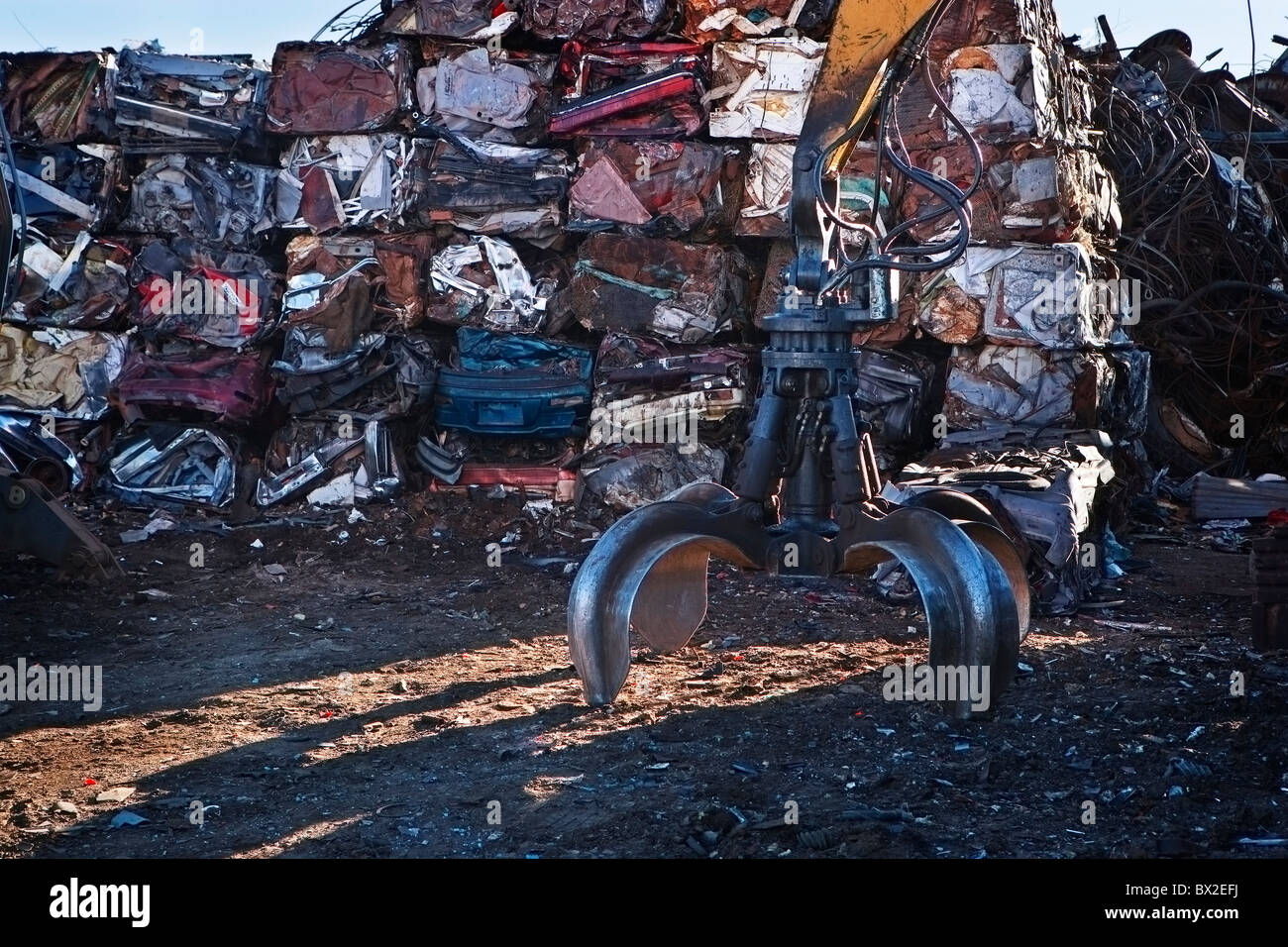 Scrap metal bales are cubed and stacked behind a giant metal claw on a ...
