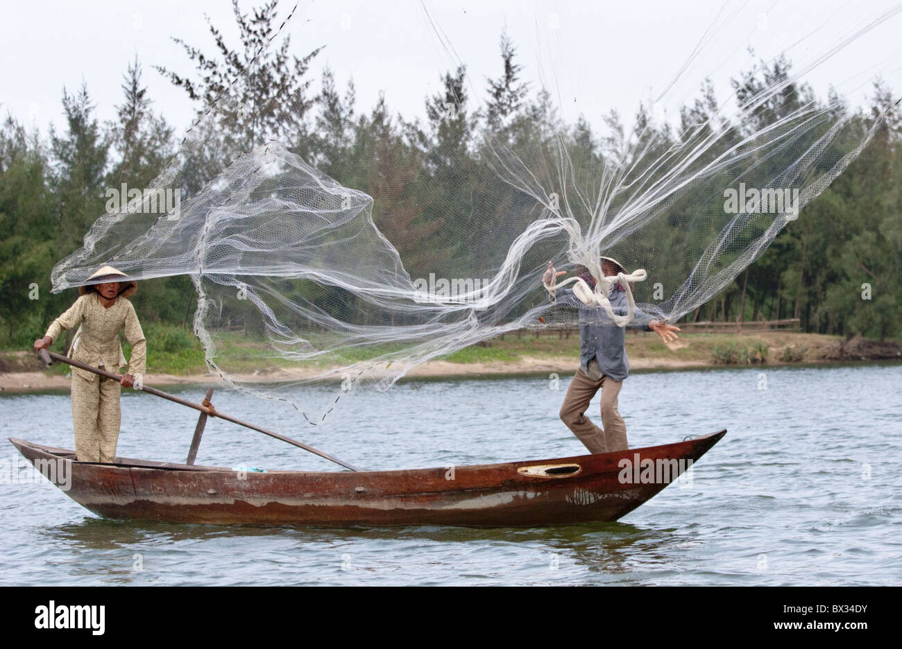 Vietnamese fisherman casting his hand-net from a small boat (rowed by ...