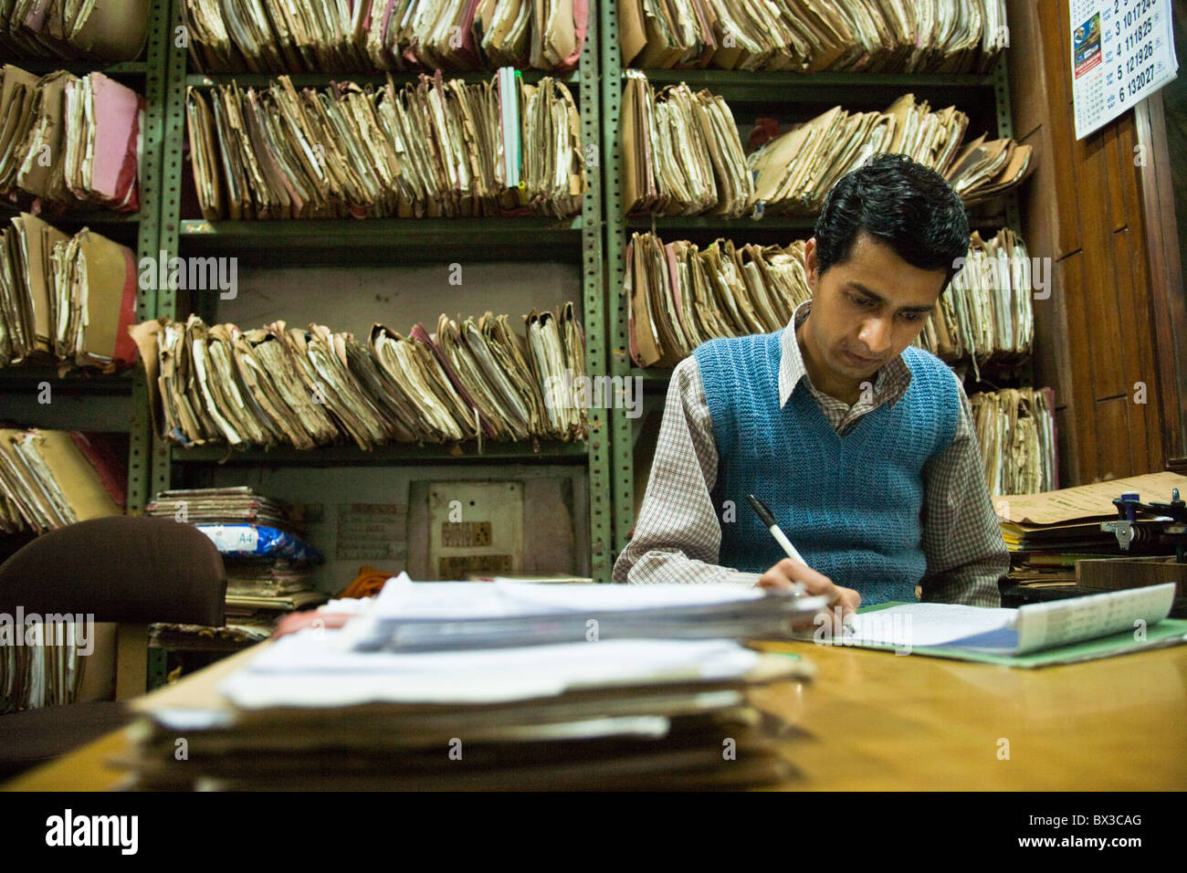 A man works in an office with piles of paperwork behind him Stock Photo ...