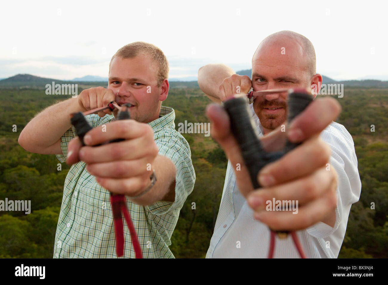 Two Men Pointing Slingshots At The Camera; Manica, Mozambique, Africa ...