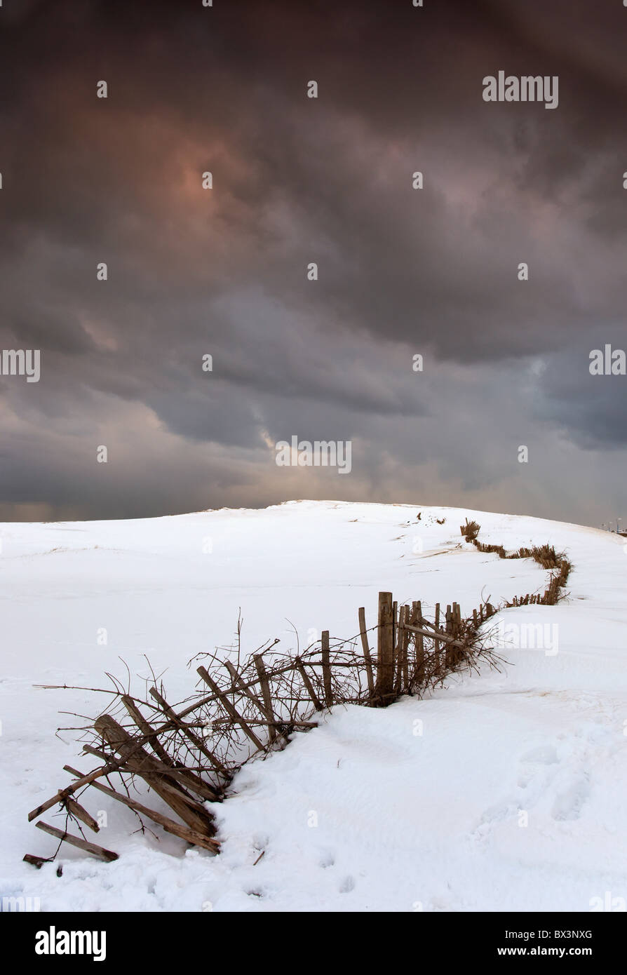 A Broken Fence Along A Snow Covered Field With Dark Clouds Overhead ...