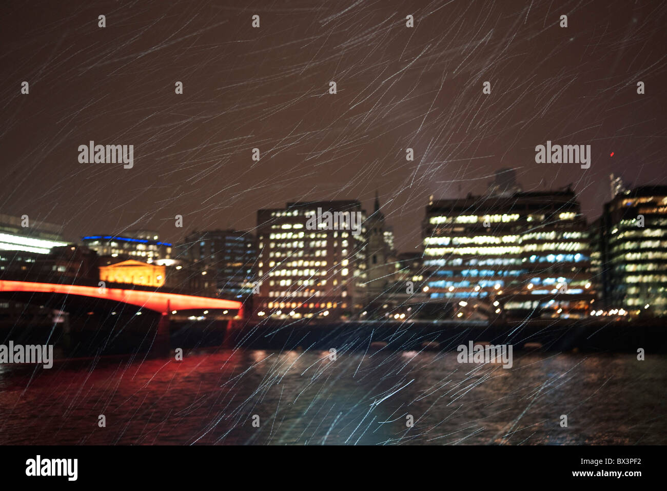 Snow falls at night in London by the river Thames on a cold snowy ...
