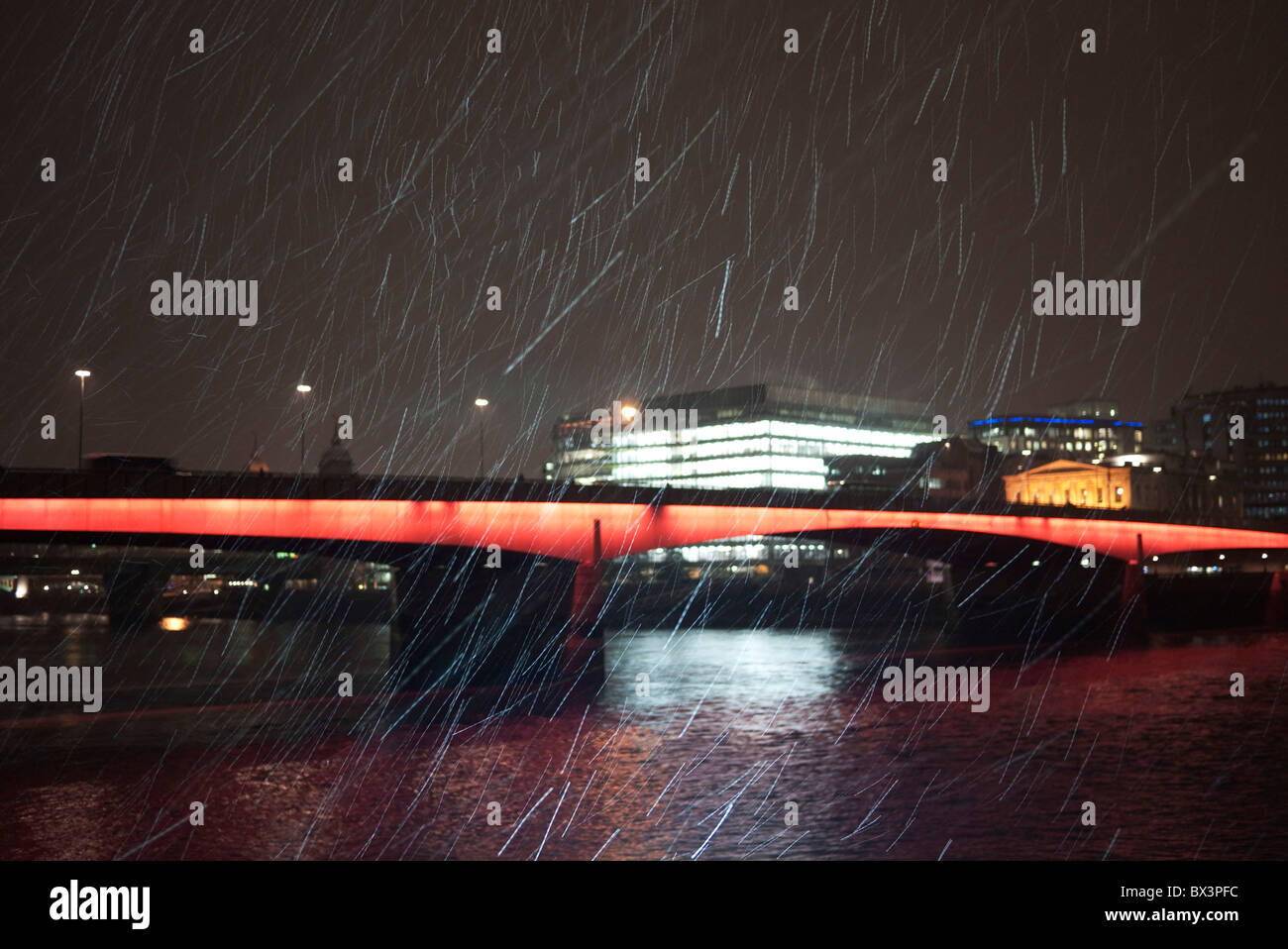 Snow falls at night in London by the river Thames on a cold snowy ...